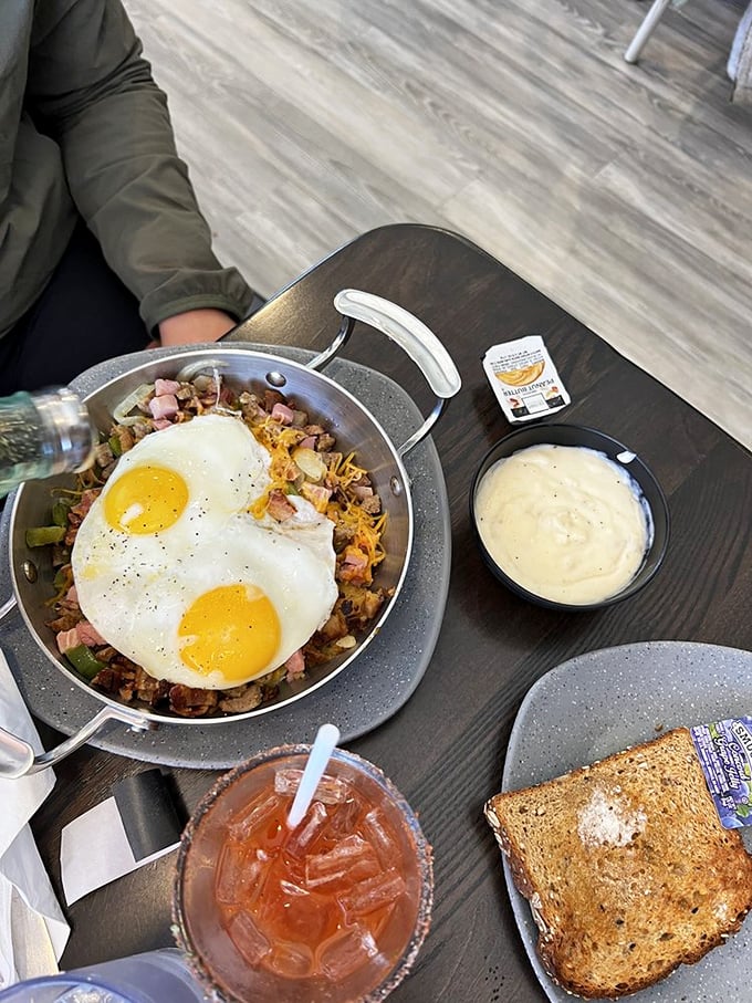 Breakfast skillet perfection: eggs sunny-side up crowning a kingdom of potatoes and ham, with toast and a Bloody Mary as loyal subjects.