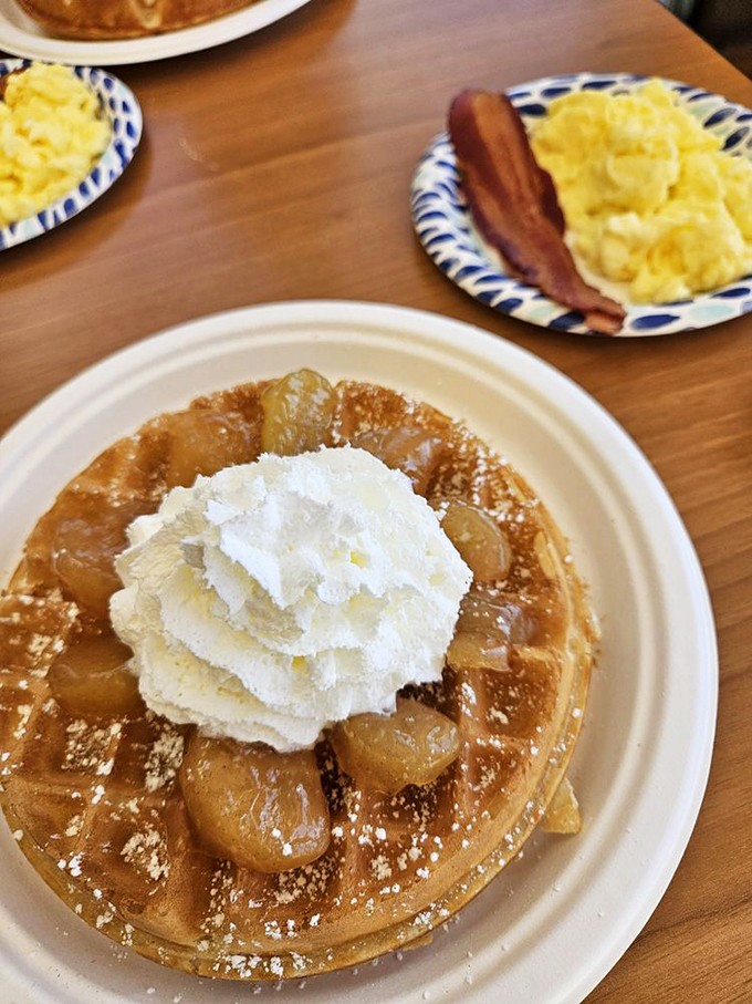 Caramelized apples cascade over a golden waffle, crowned with whipped cream—like autumn and summer decided to call a delicious truce on your plate.