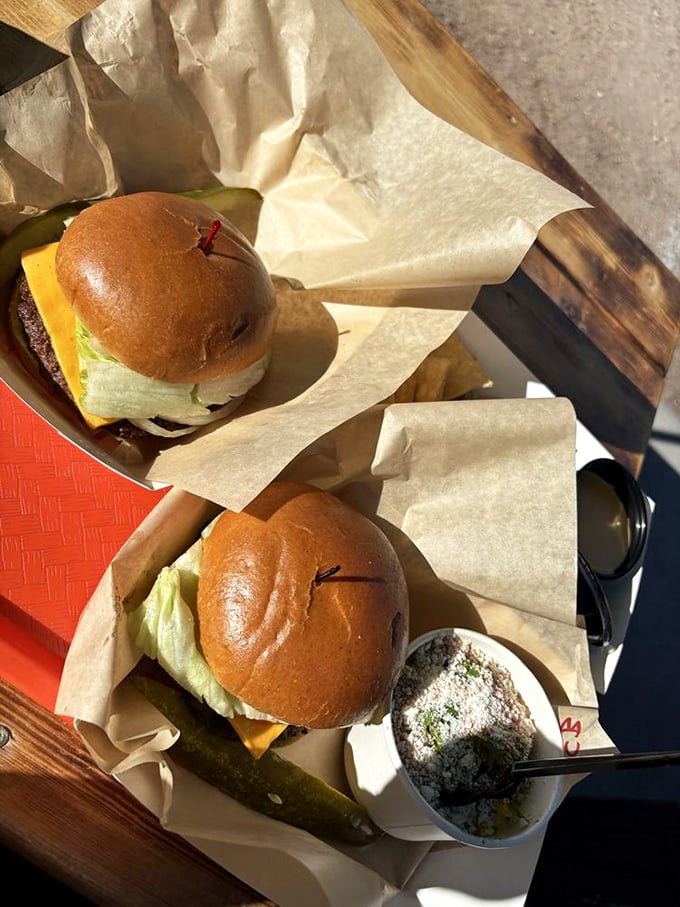 Burgers served with a pickle spear that could double as a small canoe. The paper wrapping is less packaging, more damage control.