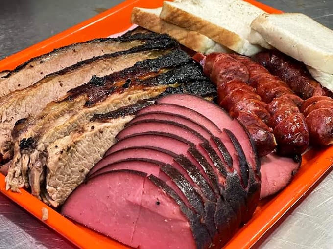 Behold the carnivore's dream team: sliced brisket with that mahogany bark, pink-centered bologna, and sausage links glistening with smoky promise.