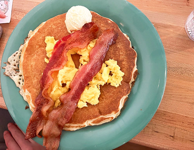 Pancake perfection with bacon strips standing guard. The butter's already melting, creating little pools of happiness you'll want to swim in.