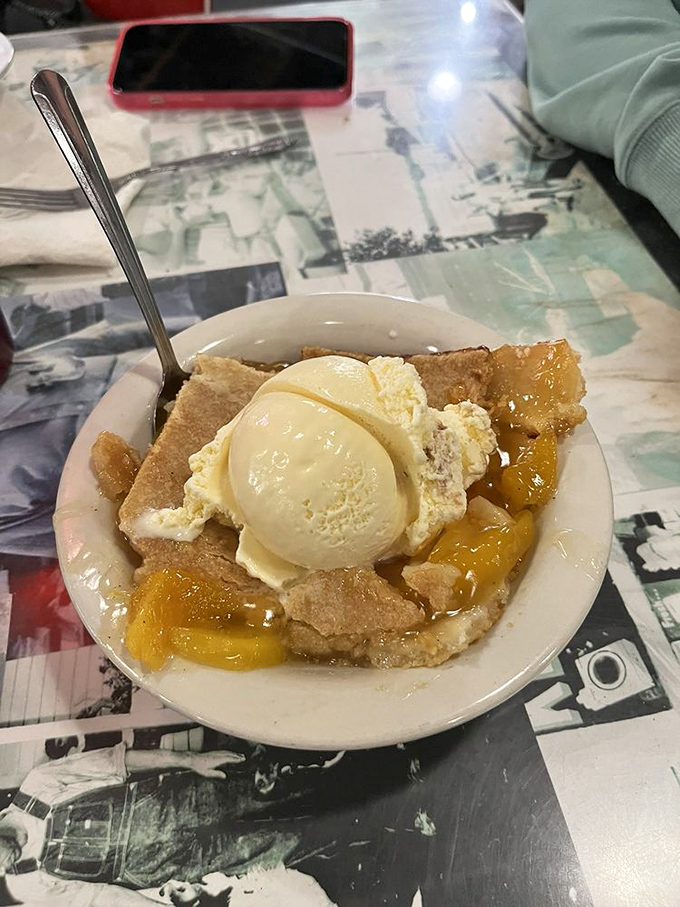 Peach cobbler that makes time stand still—warm, bubbling fruit beneath a golden crust, crowned with vanilla ice cream slowly surrendering to the heat below.