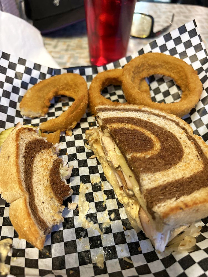 Marble rye creating the perfect swirled backdrop for this Reuben's performance. Those onion rings aren't just accessories&mdash;they're essential supporting actors in this lunchtime drama.