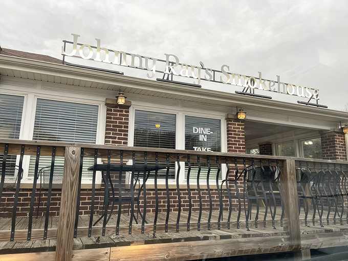The welcoming glow of Johnny Ray's Smokehouse beckons hungry travelers with its homey brick exterior and cozy wooden deck—barbecue paradise found.