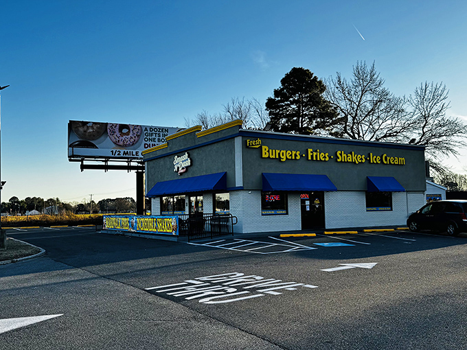 The humble roadside palace where burger dreams come true. Blue awnings and bright yellow signage beckon hungry travelers like a culinary lighthouse.