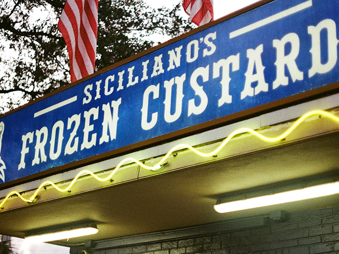 The iconic blue sign of Siciliano's stands like a beacon of frozen hope against the Florida sky, American flags fluttering above a promise of creamy perfection.
