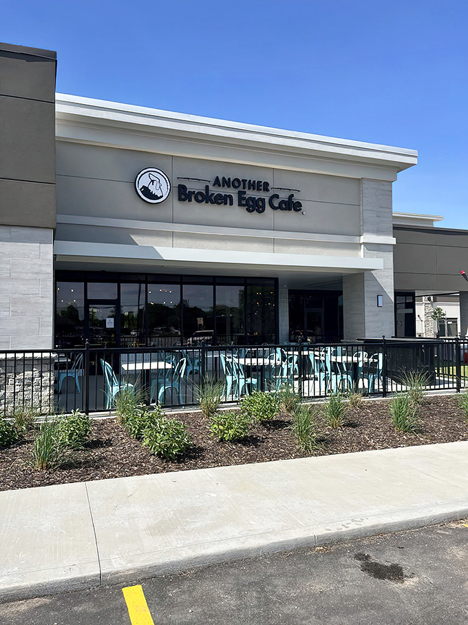 The modern facade of Another Broken Egg Cafe welcomes hungry patrons with its signature teal patio furniture—a breakfast beacon in Prairie Village.
