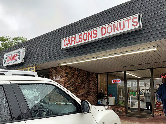 The unassuming strip mall exterior of Carlson's Donuts &ndash; where culinary magic happens behind brick walls and modest signage. Food paradise rarely announces itself with neon.