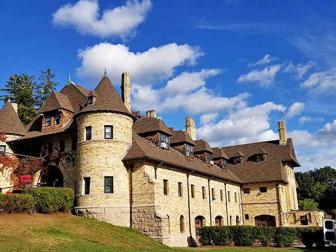 The castle-like exterior of Larz Anderson Auto Museum stands majestically against a blue sky, while a modern yellow Porsche offers a striking contrast to the historic stone facade.