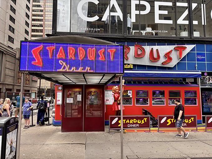 The neon-lit entrance to Ellen's Stardust Diner stands out like a Broadway marquee, promising both sustenance and showmanship in the heart of Times Square.