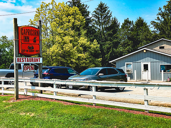 The iconic orange sign beckons hungry travelers like a burger lighthouse. This unassuming blue building houses flavor treasures worth the drive.