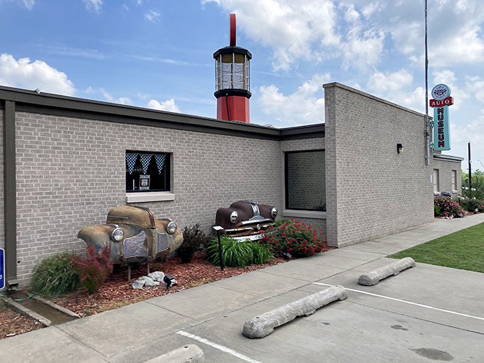 The museum's exterior features a striking lighthouse-style gas pump tower and vintage car parts artfully incorporated into the landscaping&mdash;automotive archaeology at its finest!