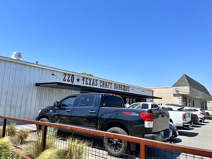 The rusted metal sign hanging above ZZQ's entrance isn't just decoration&mdash;it's a promise of authentic Texas flavor waiting just beyond those wooden picnic tables.