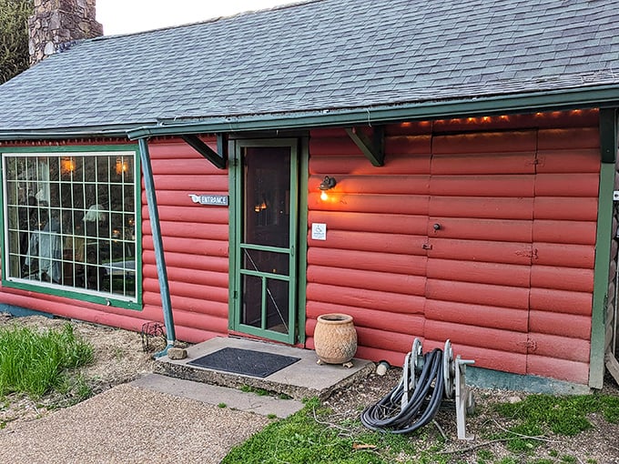 The crimson log cabin emerges from lush Ozark greenery like a storybook setting&mdash;complete with stone chimney and verdant landscaping that whispers "come on in."