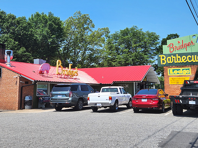 The iconic red roof and vintage sign of Red Bridges Barbecue Lodge stand as a beacon for hungry travelers. This Shelby landmark has been calling barbecue pilgrims home since 1946.