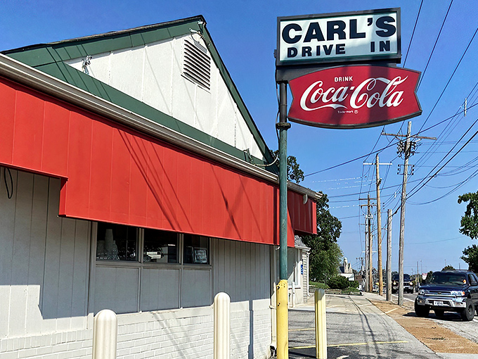 The classic red and white exterior of Carl's Drive-In stands as a time capsule on Manchester Road, beckoning burger lovers with its vintage Coca-Cola sign.