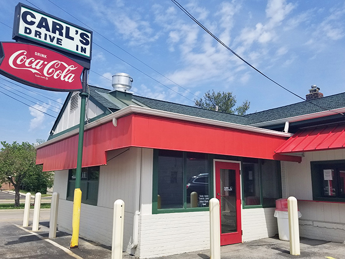 The classic red and white exterior of Carl's Drive-In stands as a time capsule on Manchester Road, beckoning burger lovers with its vintage Coca-Cola sign.