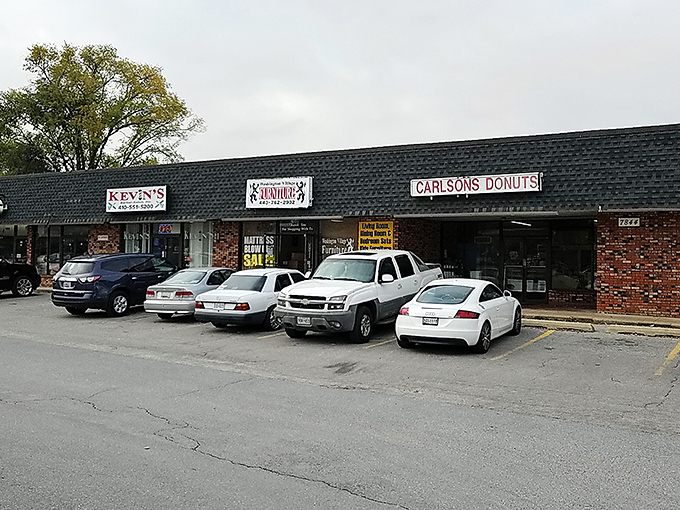 The unassuming strip mall exterior of Carlson's Donuts &ndash; where culinary magic happens behind brick walls and modest signage. Food paradise rarely announces itself with neon.