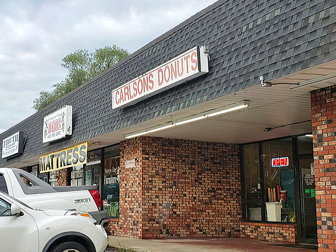 The unassuming strip mall exterior of Carlson's Donuts &ndash; where culinary magic happens behind brick walls and modest signage. Food paradise rarely announces itself with neon.