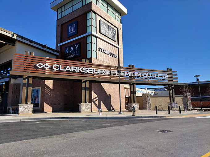 The grand entrance to Clarksburg Premium Outlets stands like a retail Colosseum, beckoning bargain hunters with promises of designer treasures within.