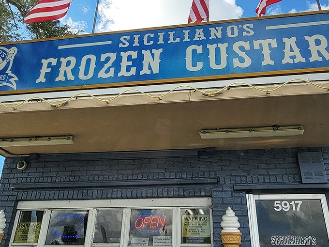 The iconic blue sign of Siciliano's stands like a beacon of frozen hope against the Florida sky, American flags fluttering above a promise of creamy perfection.