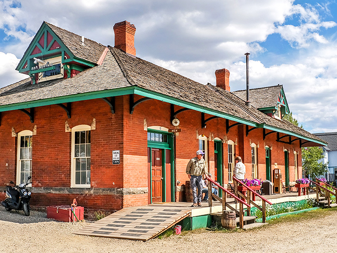 Sunlight hits this historic brick station, welcoming you to explore the porch where travelers gather under a clear mountain sky.