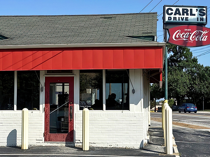 The classic red and white exterior of Carl's Drive-In stands as a time capsule on Manchester Road, beckoning burger lovers with its vintage Coca-Cola sign.