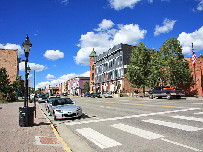 Sunlight bathes this historic mountain town as you stroll past vintage brick storefronts while a sleek silver convertible waits nearby.