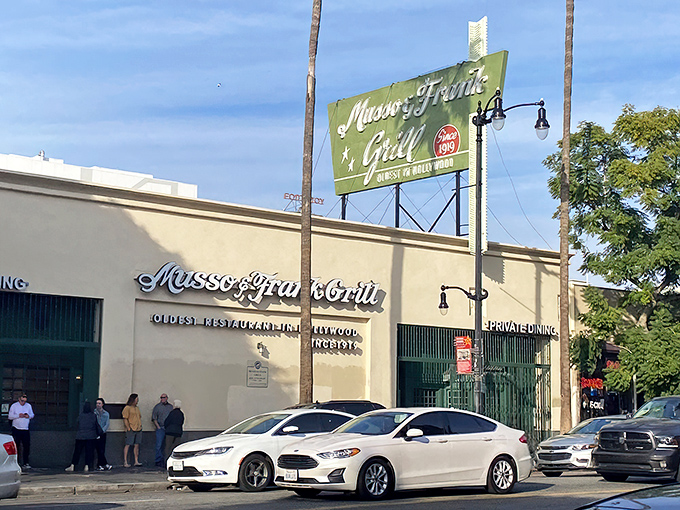 The iconic green and red sign of Musso & Frank stands proudly on Hollywood Boulevard, a beacon of culinary history amid the palm trees.