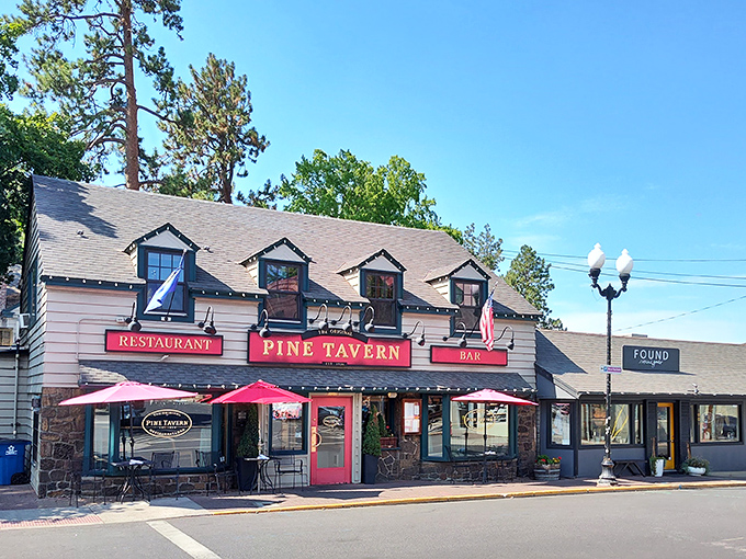 The charming exterior of Pine Tavern beckons with its classic red awning and stone facade, a timeless landmark in downtown Bend since the Great Depression era.
