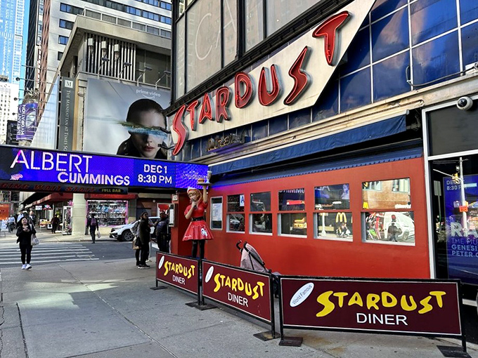The neon-lit entrance to Ellen's Stardust Diner stands out like a Broadway marquee, promising both sustenance and showmanship in the heart of Times Square.