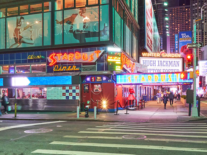 The neon-lit entrance to Ellen's Stardust Diner stands out like a Broadway marquee, promising both sustenance and showmanship in the heart of Times Square.