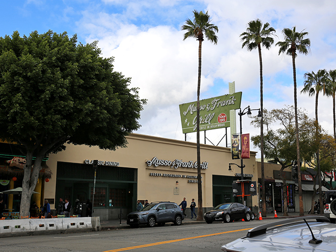 The iconic green and red sign of Musso & Frank stands proudly on Hollywood Boulevard, a beacon of culinary history amid the palm trees.
