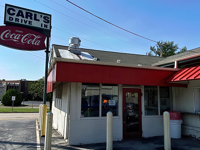 The classic red and white exterior of Carl's Drive-In stands as a time capsule on Manchester Road, beckoning burger lovers with its vintage Coca-Cola sign.