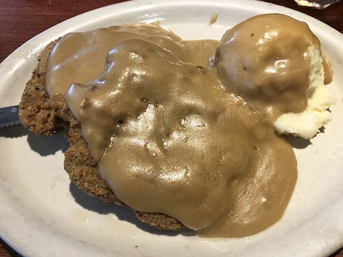 Country fried steak swimming in gravy&mdash;where crispy exterior meets tender interior in a pool of peppery paradise. Southern comfort on a plate.