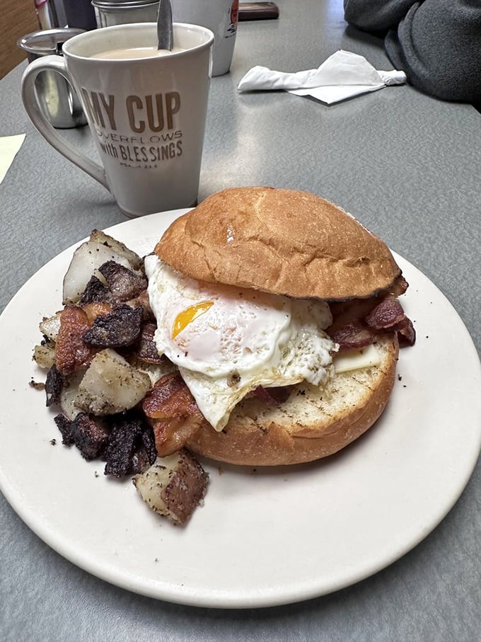 Breakfast sandwich architecture at its finest – a perfectly fried egg perched atop bacon, all nestled in a fresh roll. The home fries look like they're auditioning for a food magazine.