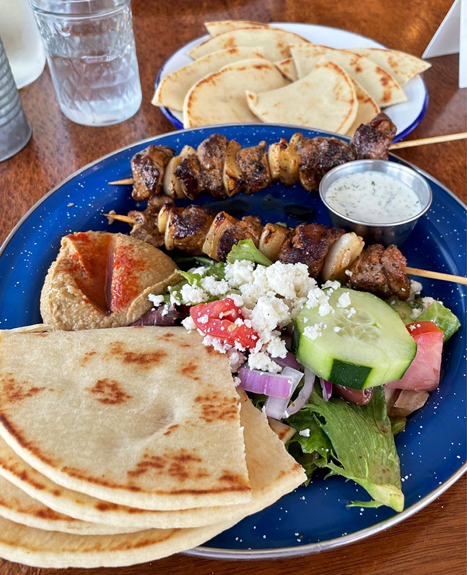 Skewers of perfectly seasoned meat alongside warm pita and fresh Greek salad—proof that sometimes the simplest combinations are the most magnificent.