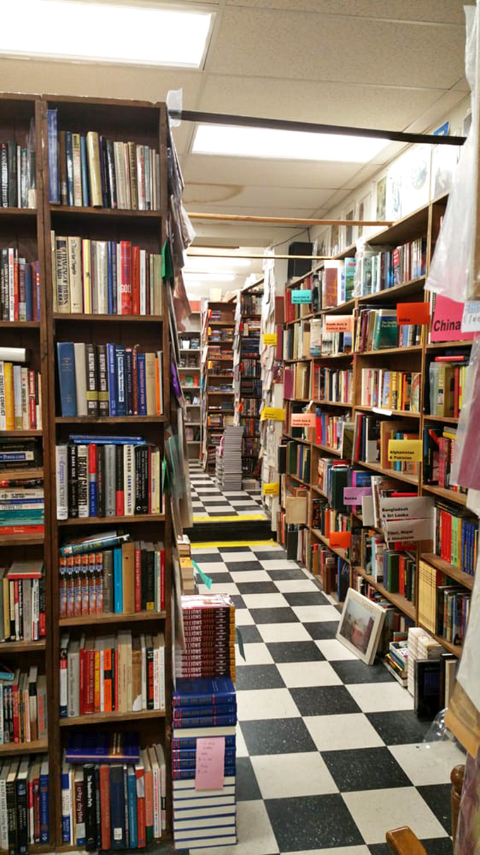 The non-fiction section stretches toward infinity, with bright tags organizing human knowledge into digestible chunks. The checkered floor guides your journey.