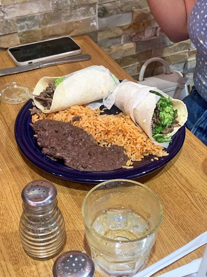 Two soft tacos cradling their fillings like precious cargo, sharing plate space with rice and beans in perfect culinary harmony.