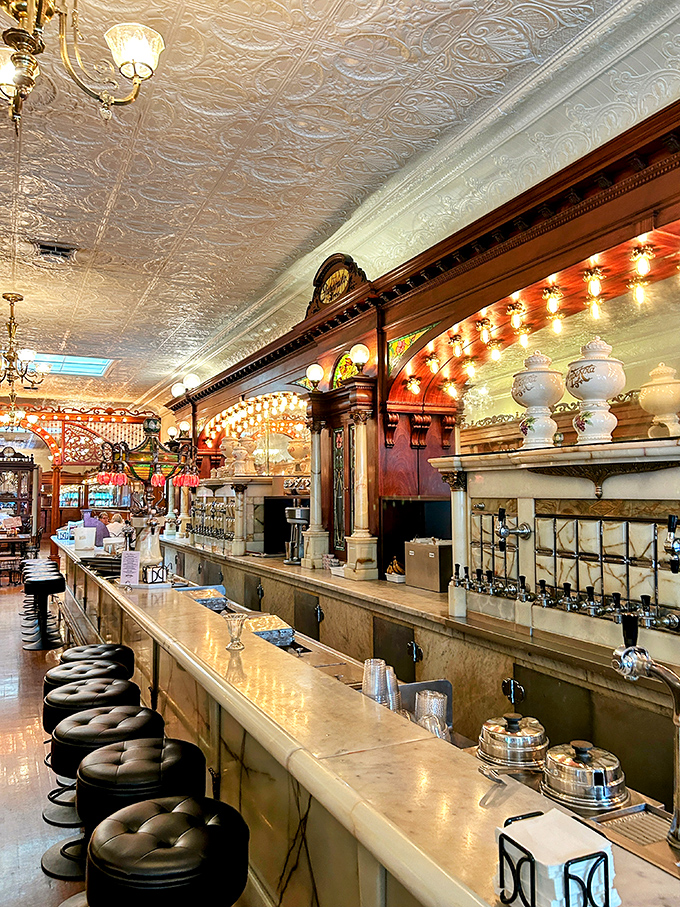 Bar stools lined up like loyal soldiers, ready for the next ice cream commander. That marble counter has supported more elbows than a busy tailor.