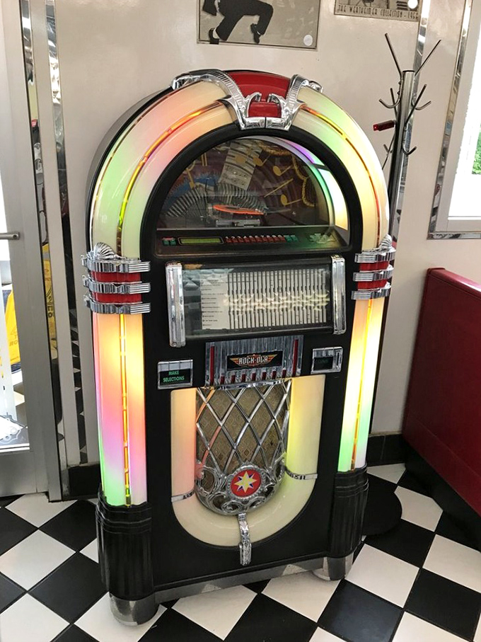 The jukebox stands like a neon-lit altar to simpler times, when quarters bought happiness and Buddy Holly ruled the airwaves.