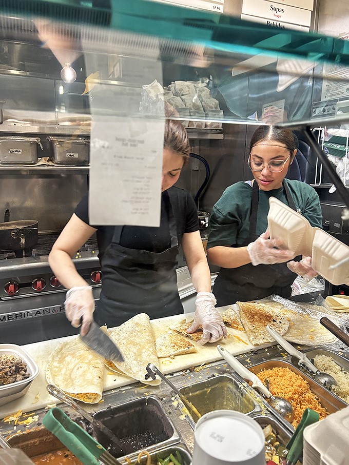 Behind the glass, culinary choreography unfolds – fresh ingredients lined up like eager actors waiting for their moment to shine in your burrito.