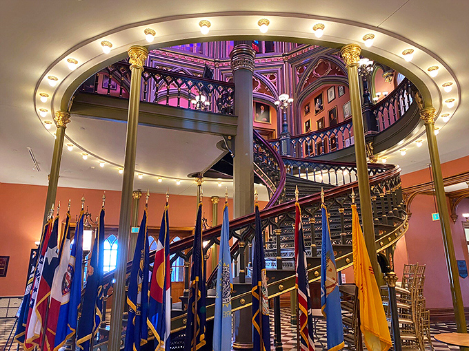 The showstopping spiral staircase winds upward beneath a canopy of flags, its wrought iron details showcasing 19th-century craftsmanship at its finest.