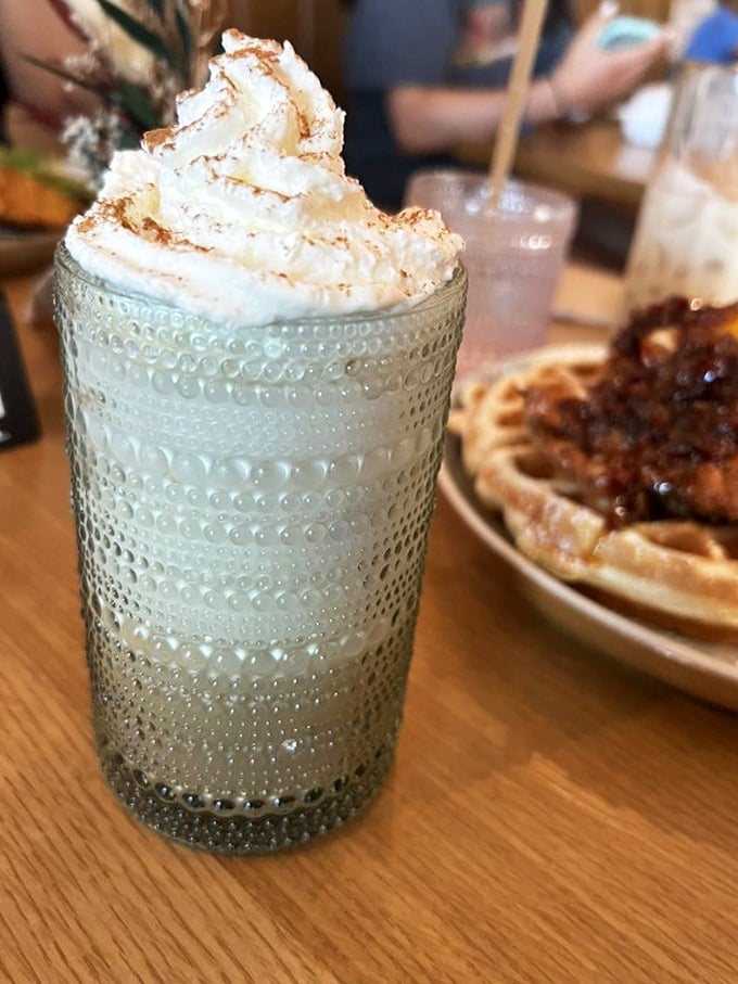 Whipped cream mountain meets textured glass&mdash;this isn't just a drink, it's a morning celebration with a waffle cameo in the background.