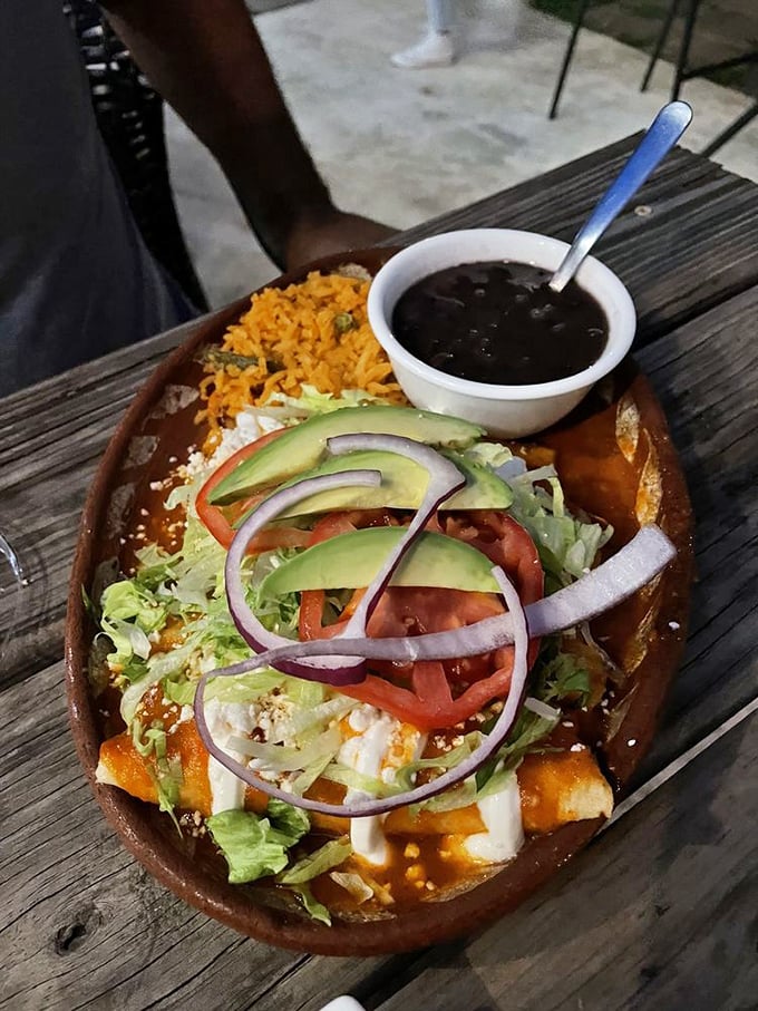 A clay dish cradling enchiladas swimming in authentic sauce, topped with fresh veggies and creamy avocado. Comfort food elevated.