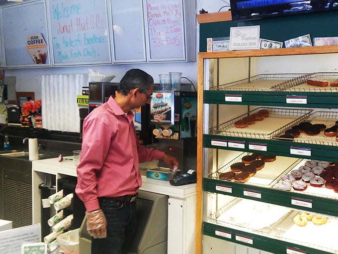 The maestro at work, where every transaction is accompanied by the symphony of fresh donuts being arranged. Those gloves handle more happiness than Santa on Christmas Eve.