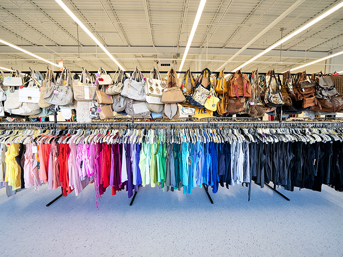 An aerial view of handbags suspended like colorful stalactites above a rainbow sea of meticulously organized clothing.