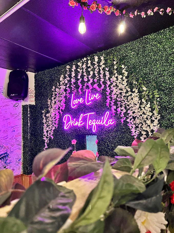 The "Love Live Drink Tequila" neon sign isn't just decoration—it's a life philosophy against a backdrop of artificial flowers that somehow works perfectly.