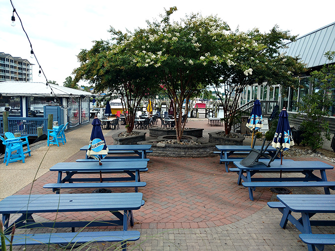 Blue picnic tables under string lights create an outdoor oasis where river breezes carry tantalizing aromas from the kitchen.
