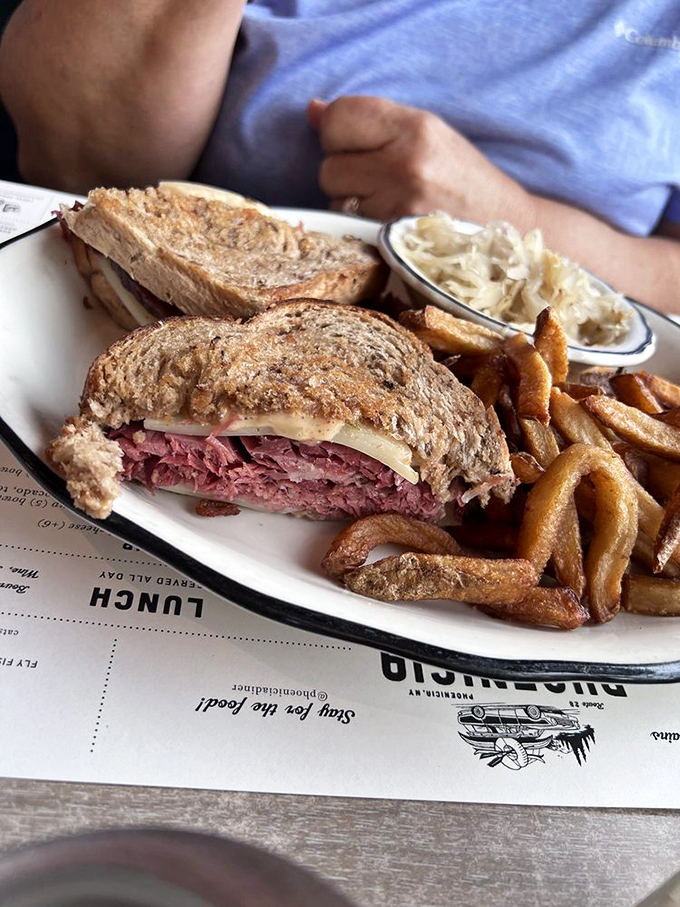 The Reuben sandwich in its natural habitat—surrounded by crispy fries and anticipation. Each layer visible like delicious geological strata of flavor.